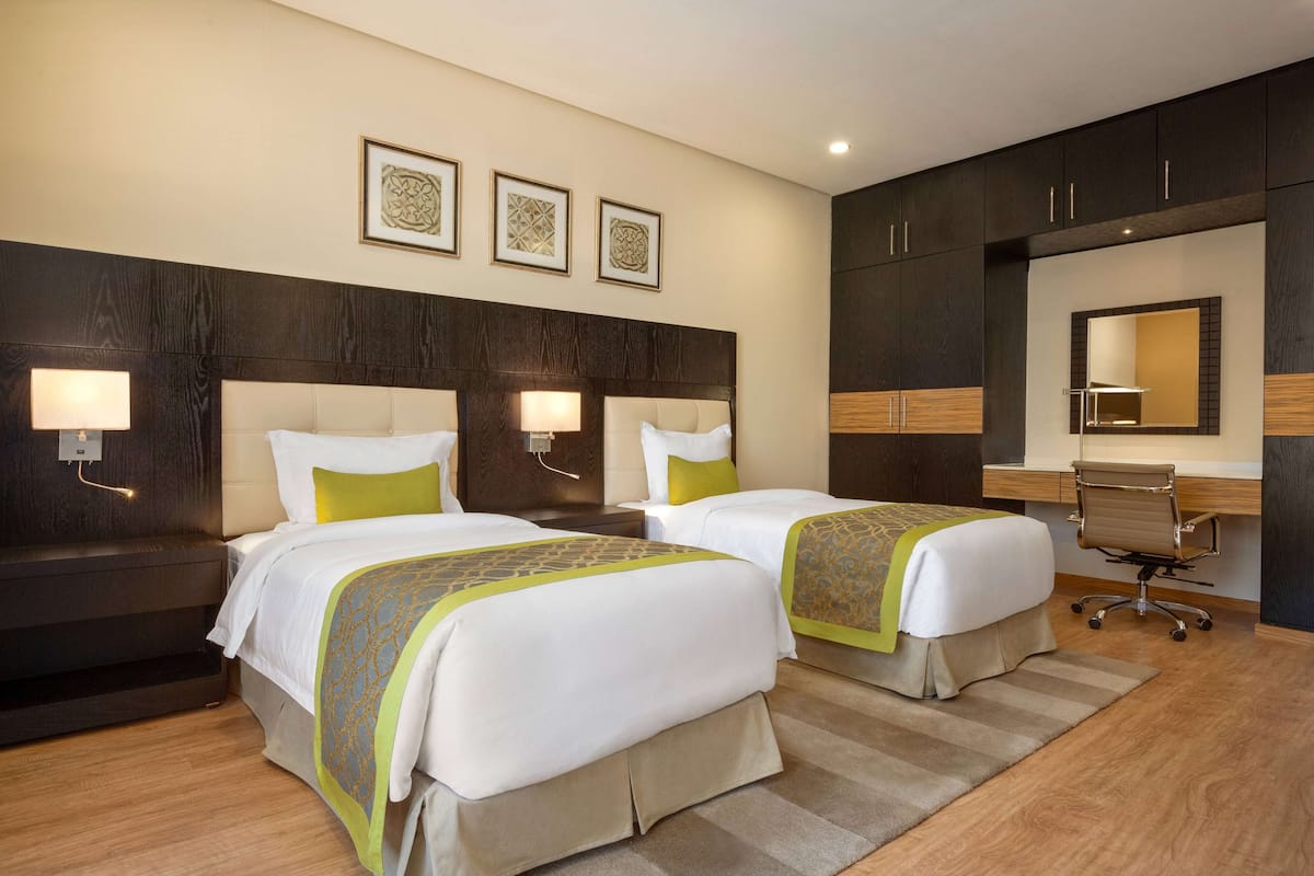 Quarto de hotel com duas camas, uma mesa e uma cadeira.