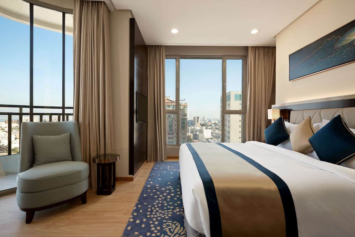 Quarto de hotel com uma cama grande, uma cadeira, uma televisão e vista para a cidade.