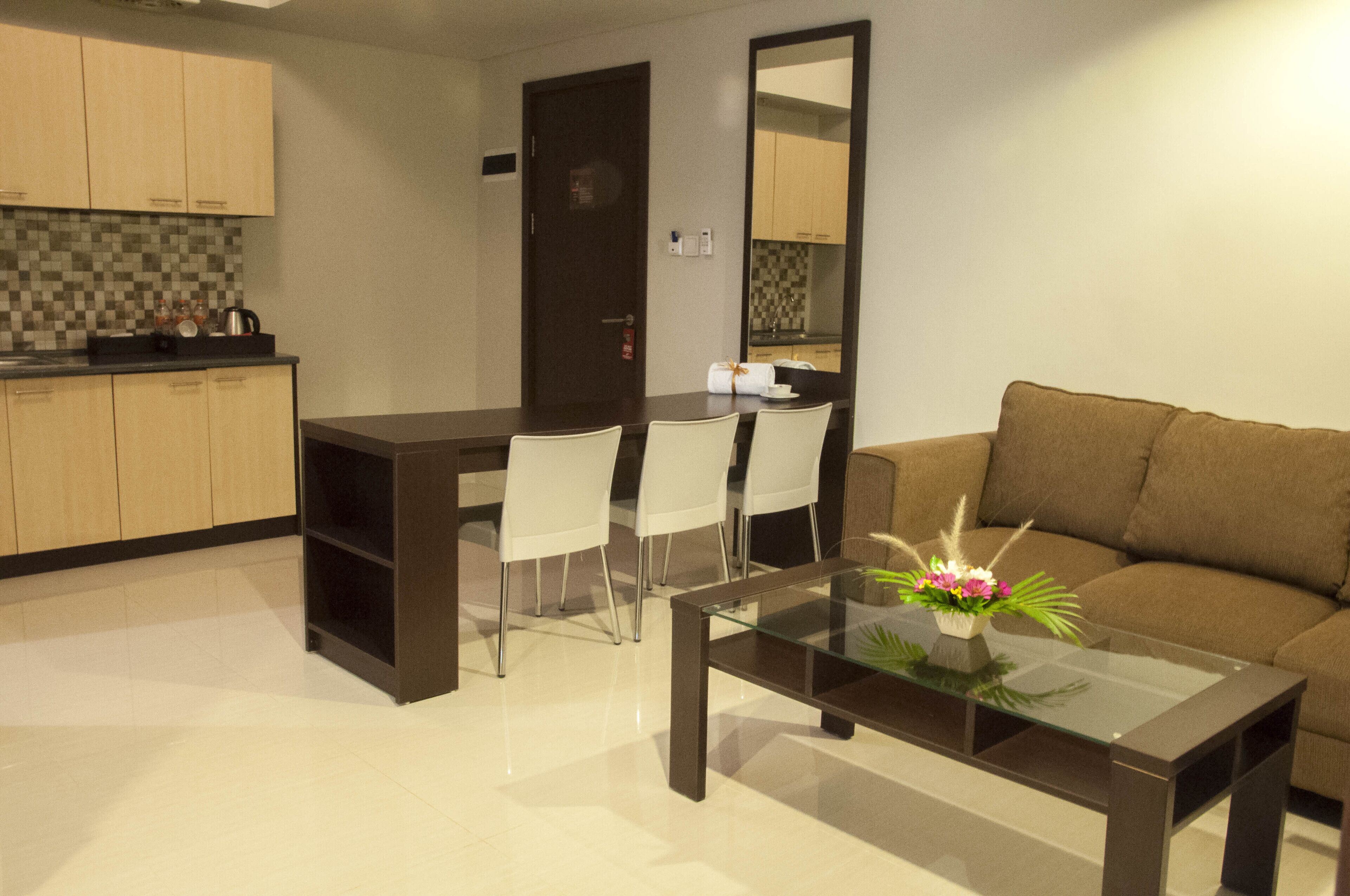 Uma sala de estar moderna com uma mesa de centro de vidro, um sofá marrom e um espaço de jantar com uma mesa de madeira escura e cadeiras brancas.