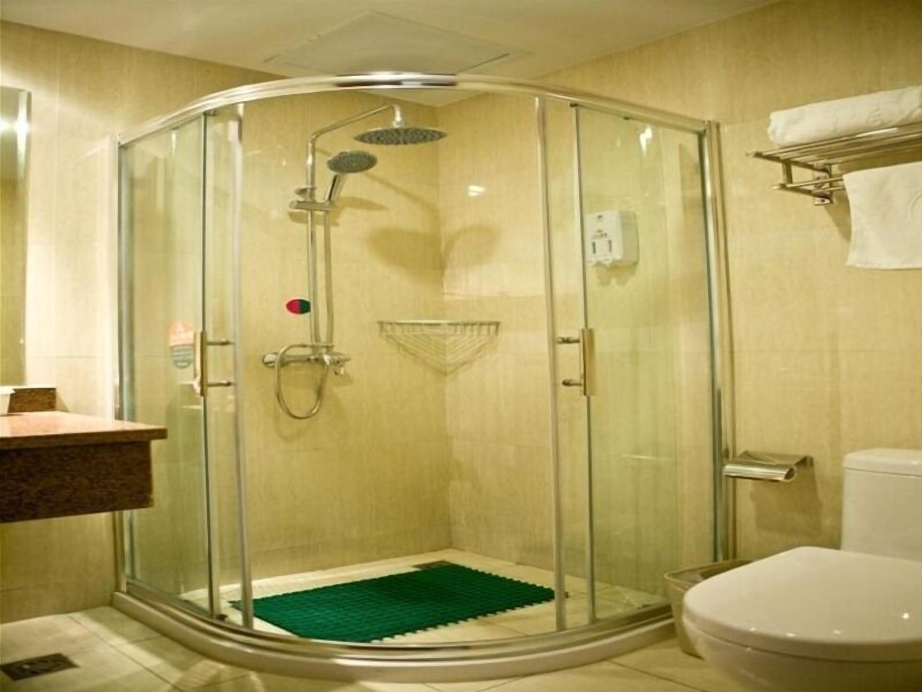 Um chuveiro com divisória de vidro, um tapete verde, um vaso sanitário e um porta-toalhas.