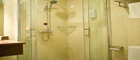 Um chuveiro com divisória de vidro, um tapete verde, um vaso sanitário e um porta-toalhas.