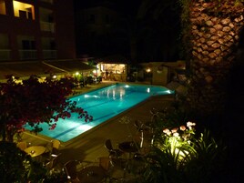 Área de piscina à noite, com espreguiçadeiras e um bar.