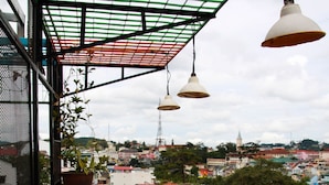 Uma varanda com vista para o horizonte urbano, com guarda-corrimão de metal, um banco de madeira e um vaso de planta.