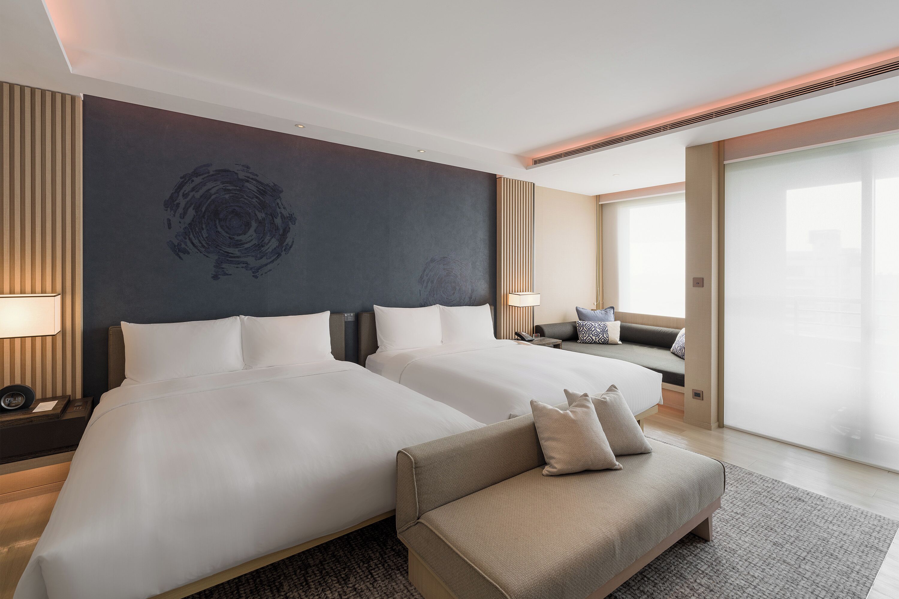 Quarto de hotel com duas camas, um sofá, uma obra de arte na parede e uma janela grande.