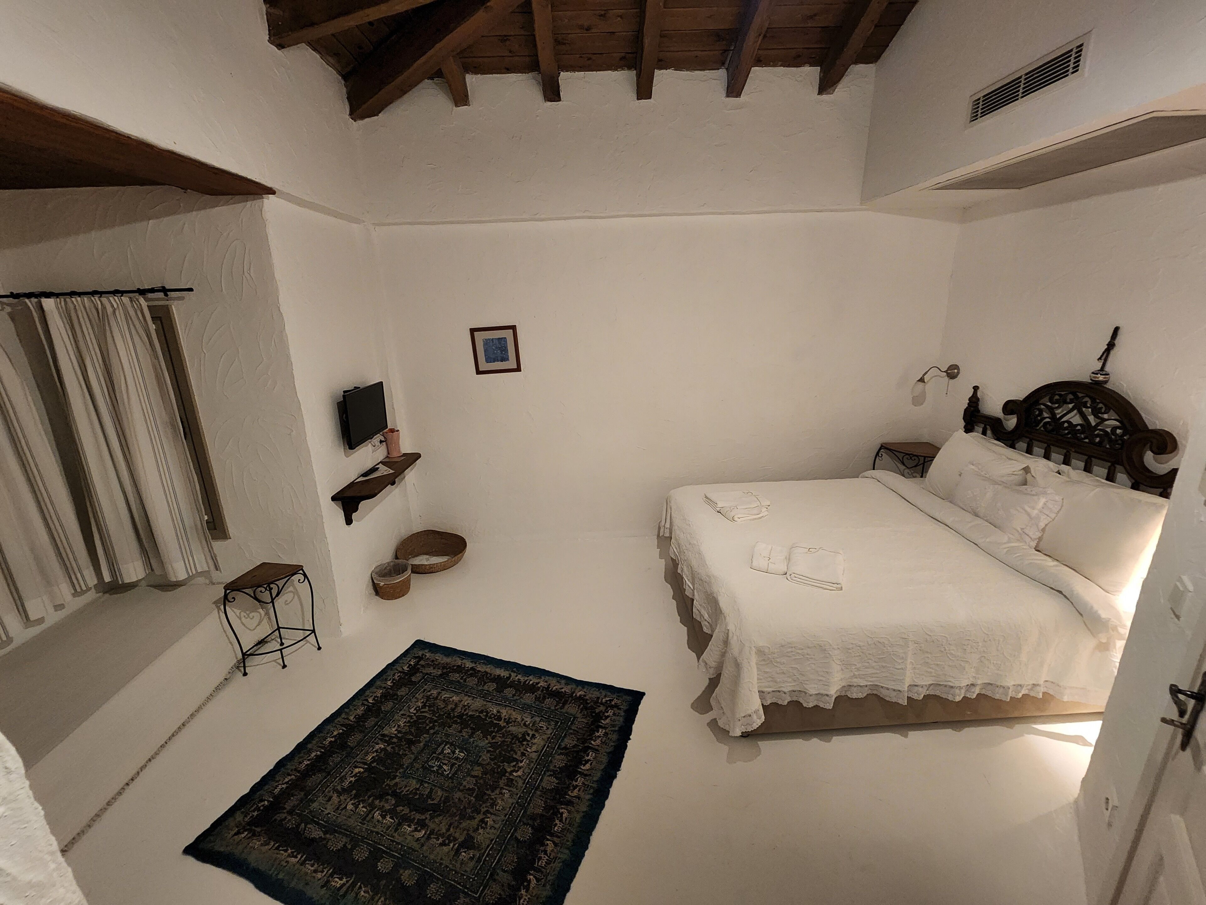 Quarto com cama, televisão, mesinha, tapete e janela com cortinas.