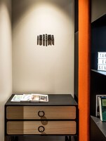Quarto com mesa de cabeceira de madeira, uma revista e uma estante com livros e uma lightbox exibindo a frase 'TAKE ENJOY & ENJOY'.