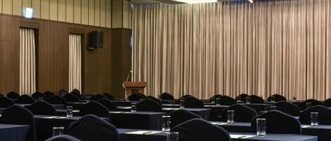 Uma sala de conferências com mesas, cadeiras e um pódio dispostos em fileiras.