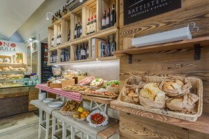 Um balcão de padaria com diversos pães e doces, uma área de exposição de vinhos com garrafas, e uma placa com a inscrição 