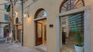 Uma rua estreita com um prédio que tem uma porta de madeira e uma janela com uma planta em vaso.