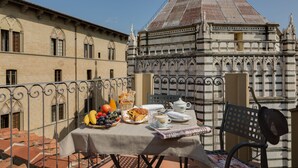 Mesa posta com itens de café da manhã em uma varanda com vista para um edifício histórico.