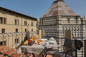 Mesa posta com itens de café da manhã em uma varanda com vista para um edifício histórico.