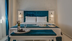 Cama bem arrumada com cabeceira azul-turquesa, roupa de cama branca e mesa de cabeceira com uma garrafa de vinho e uvas.