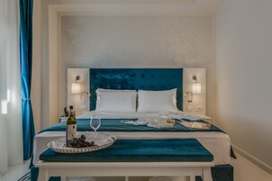 Cama bem arrumada com cabeceira azul-turquesa, roupa de cama branca e mesa de cabeceira com uma garrafa de vinho e uvas.
