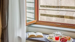 Uma bandeja de café da manhã com um livro, um bule, uma xícara, um copo de suco e doces em um parapeito de janela.