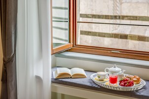 Uma bandeja de café da manhã com um livro, um bule, uma xícara, um copo de suco e doces em um parapeito de janela.
