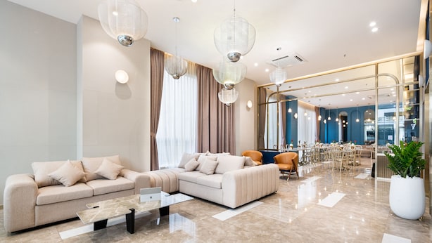 Um lobby de hotel moderno com um sofá bege, uma mesa de centro e uma área de refeições com cadeiras e mesas.