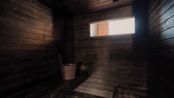 Interior de uma cabana de madeira com uma pequena janela, um balde de metal e um banco de madeira.