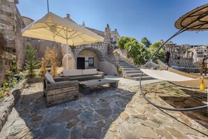 Um pátio de pedra com mobiliário para área externa, um espaço coberto e uma escadaria que leva a um edifício.
