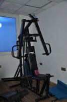 Uma academia com um equipamento de exercício multifuncional, um banco e um tapete azul no chão.