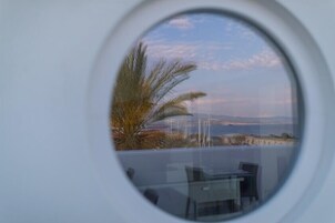 Janela circular com vista para uma mesa e cadeiras lá fora.
