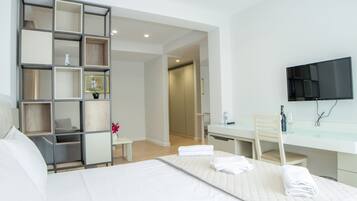 Quarto de hotel moderno com cama, escrivaninha, cadeira, televisão e guarda-roupa.