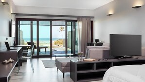 Quarto de hotel moderno com uma cama grande, televisão, secretária com um computador portátil e vista para a praia.