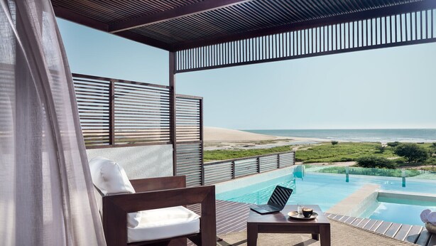Uma varanda com vista para a praia, uma piscina e uma cadeira.