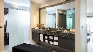 Uma casa de banho moderna com toucador de mármore, um espelho grande e um banco preto.