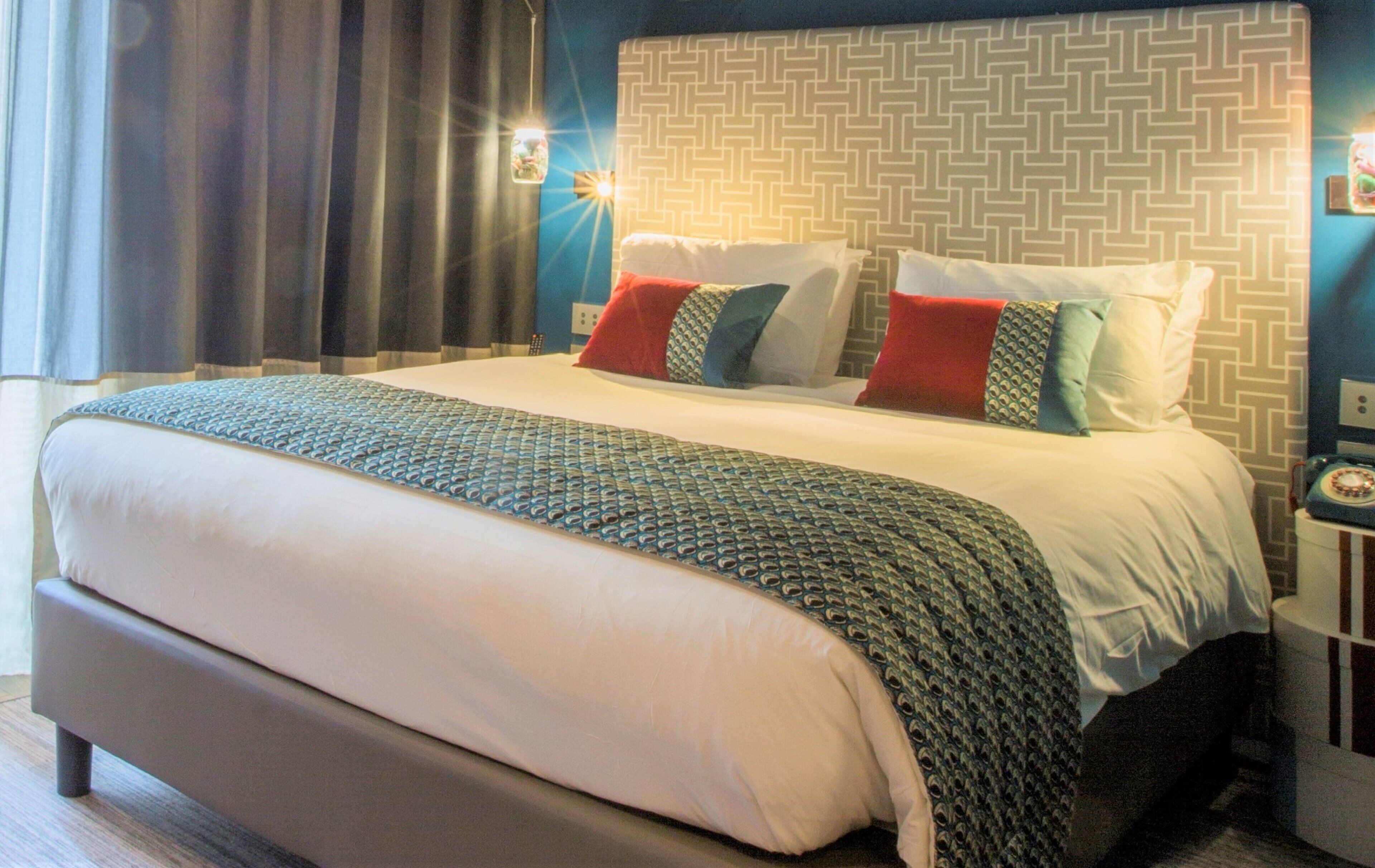Quarto de hotel com uma cama grande, cabeceira estampada com padrão geométrico e duas luminárias de cabeceira.