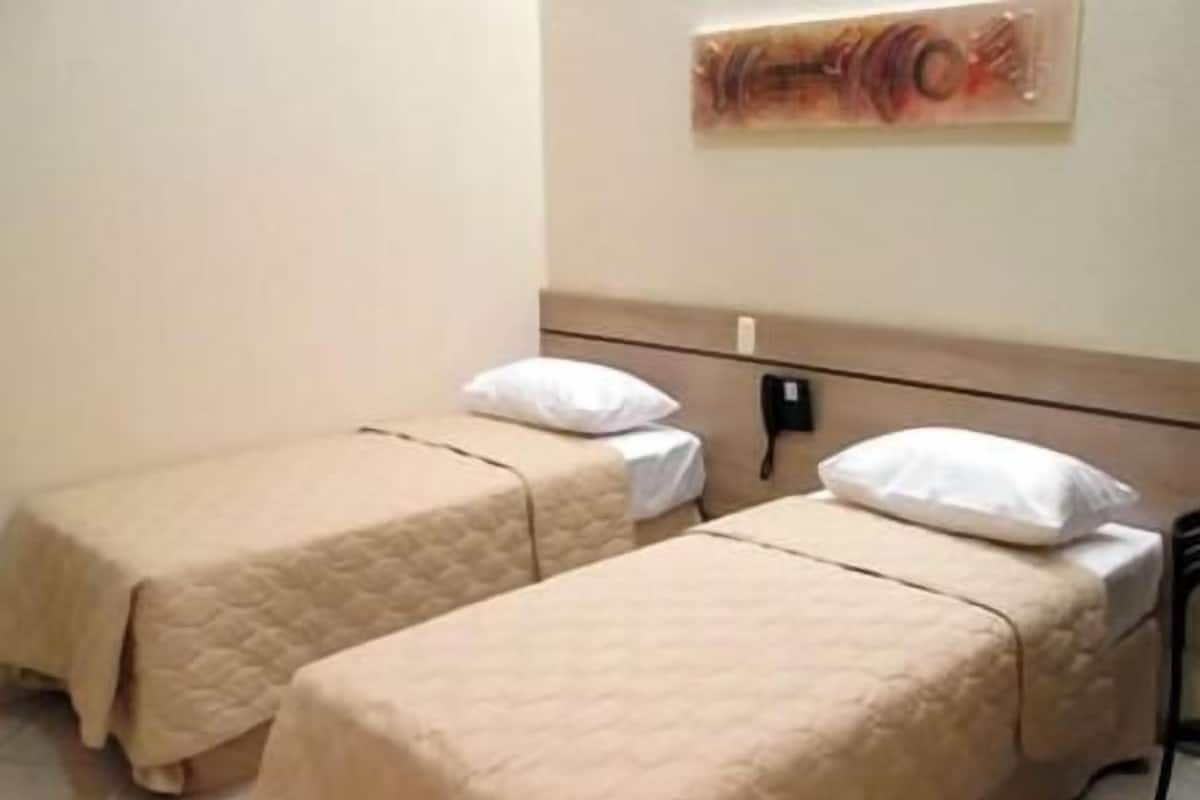 Duas camas de solteiro com roupa de cama branca num quarto.