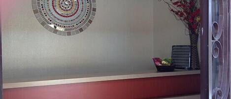 Um quarto com um painel de mosaico circular na parede, um banco vermelho e bege, e um vaso com flores.