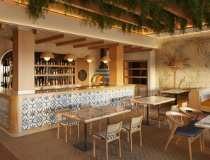 Uma área de bar com painel atrás do balcão revestido de azulejos, balcão de madeira e disposição de mesas e cadeiras.