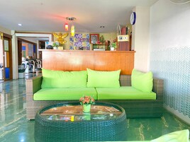 Um hall com um sofá verde, uma mesa de centro de vime redonda e um balcão de recepção.