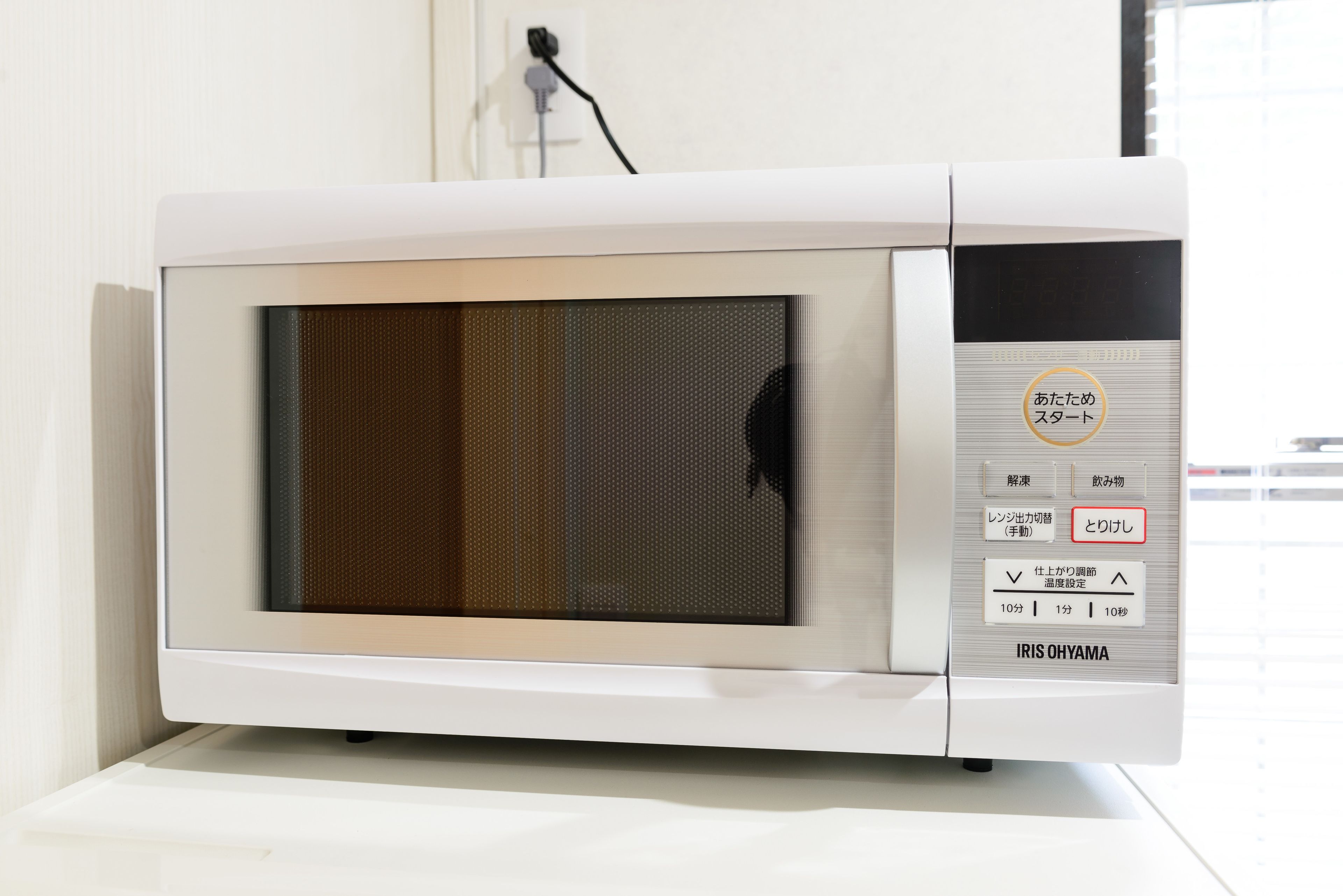 Um micro-ondas com visor digital e painel de controle, sobre uma bancada branca.