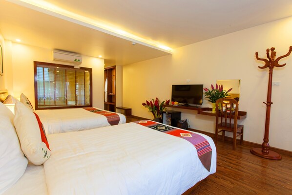 Quarto de hotel com duas camas, uma escrivaninha com computador, televisão e um cabideiro.