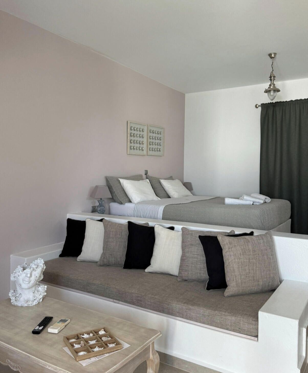 Quarto compacto com sofá-cama, uma mesinha com um controle remoto e um objeto decorativo, e luminária de teto.
