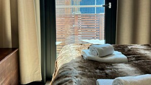 Quarto com cama, janela e vista para um edifício e paisagem.