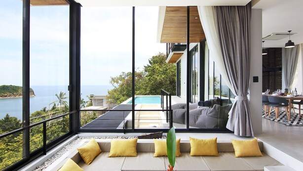 Uma sala de estar moderna com uma grande janela com vista para uma piscina e o mar.