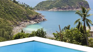 Piscina com vista para a paisagem costeira, incluindo uma praia e uma colina com vegetação densa.