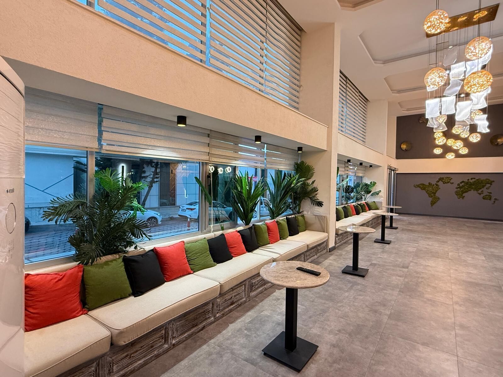 Um hall moderno com um longo banco, pequenas mesas e grandes janelas com persianas.