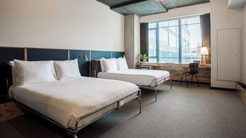Quarto de hotel com duas camas, uma escrivaninha, uma cadeira e uma janela grande com persianas.