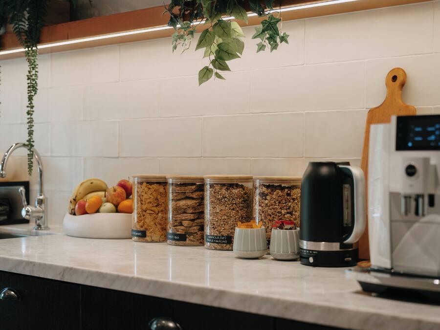 Uma bancada de cozinha com uma fruteira, potes de lanches, chaleira e cafeteira.