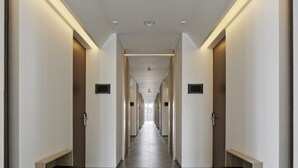Um corredor comprido e estreito com design moderno, apresentando um candelabro central e uma série de portas em ambos os lados.