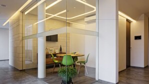 Um interior moderno com divisória de vidro, uma mesa redonda com cadeiras e um vaso de planta.