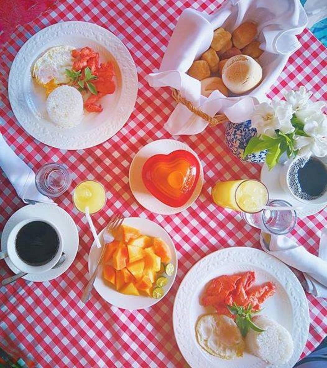 Uma mesa posta com pratos de comida, incluindo ovos, frutas e pão, sobre uma toalha quadriculada vermelha e branca.
