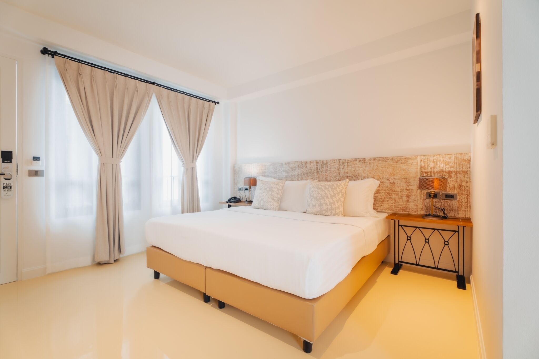 Quarto de hotel moderno com uma cama grande, uma mesa de cabeceira com luminárias e uma cabeceira com padrão de tijolos.