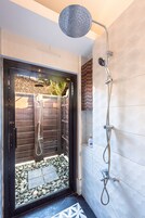 Uma área de chuveiro moderna com porta de vidro, chuveiro de teto e chuveiro manual.