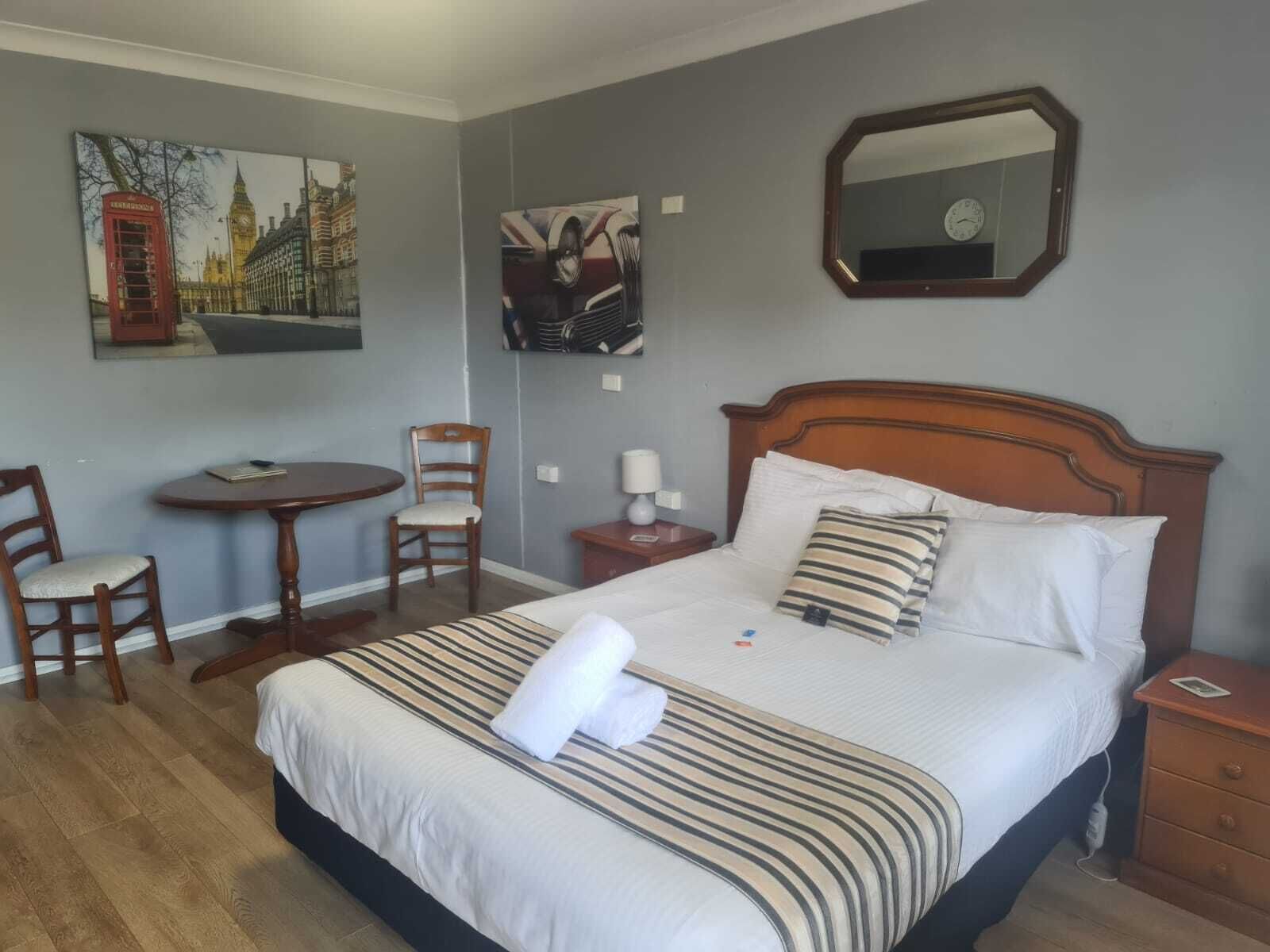 Quarto de hotel com uma cama, uma cadeira, uma mesa, um espelho e obras de arte nas paredes.