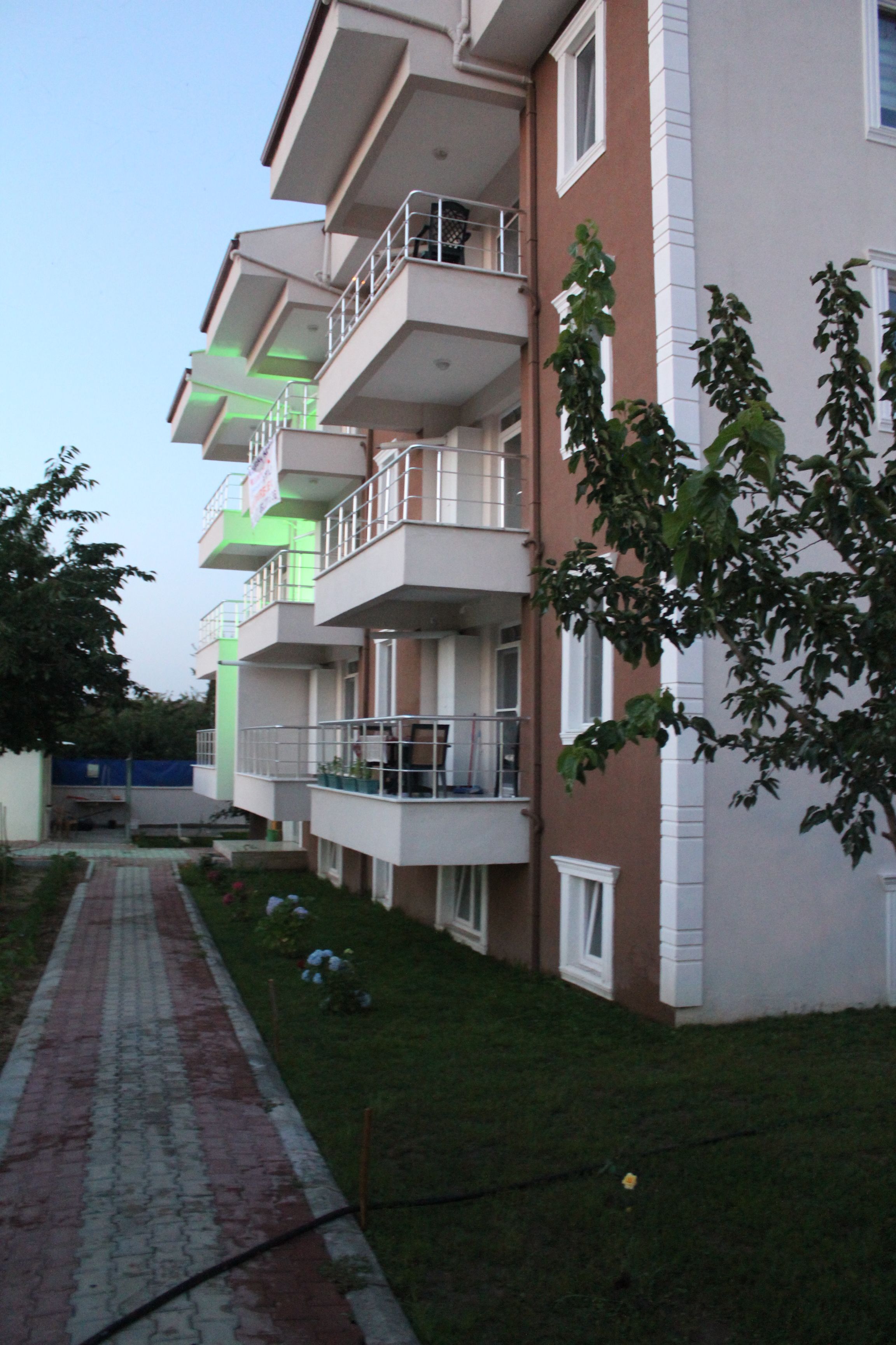 Um edifício residencial com vários andares, varandas, um caminho pavimentado e uma área ajardinada.