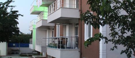 Um edifício residencial com vários andares, varandas, um caminho pavimentado e uma área ajardinada.